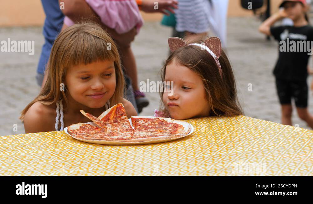 Two children girls eat street food pizza on festival day outdoors ...