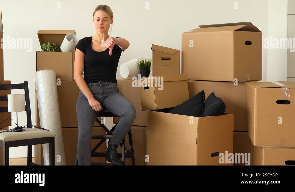 An unhappy moving woman sits on a chair in an empty apartment, shakes ...