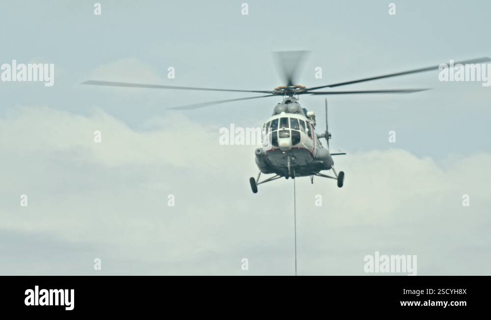 A helicopter flying in the sky at overcast weather - the cable hangs ...