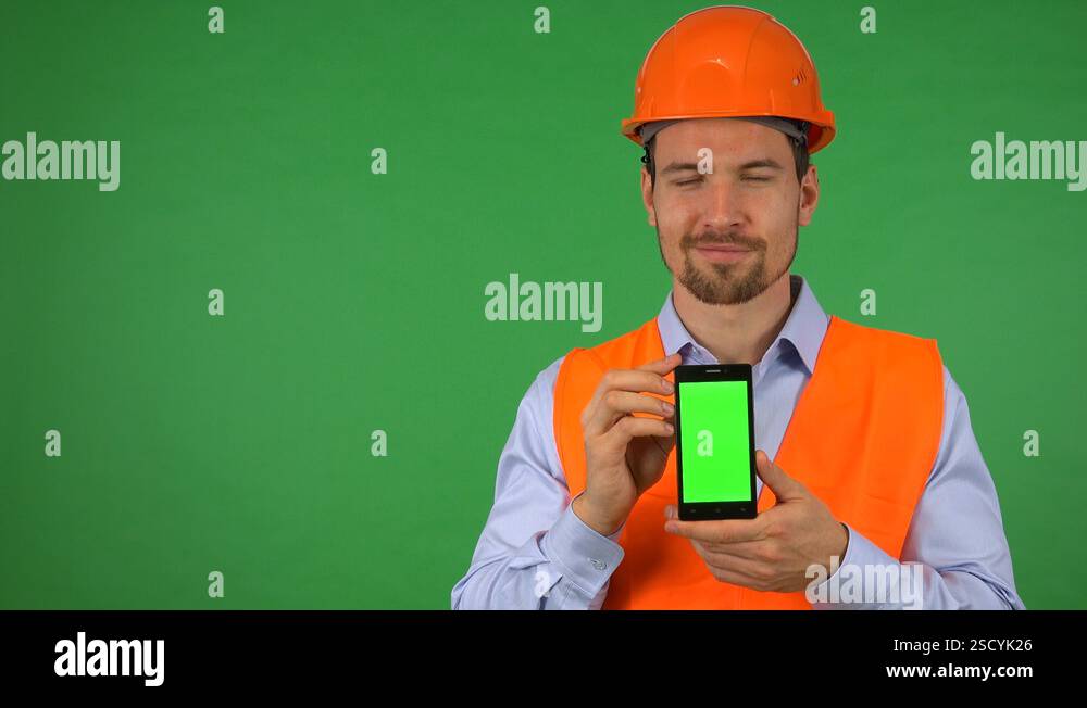 A young handsome construction worker shows a smartphone with green ...