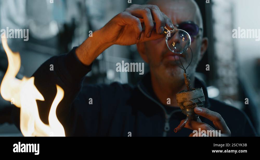A glass blower is working on an art piece of glass from crystal in a ...