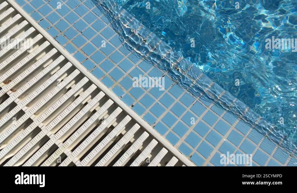 Wavy clear water in a blue tiled swimming pool with white drain grill ...