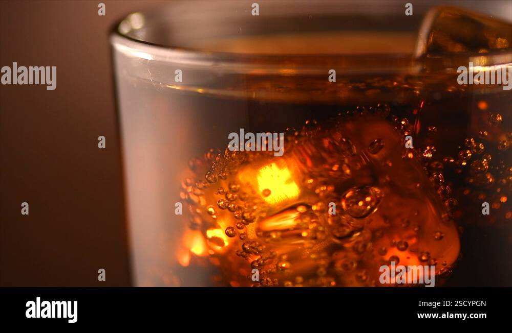 Coke with ice cubes closeup. Glass of fizzy cola rotated over brown ...