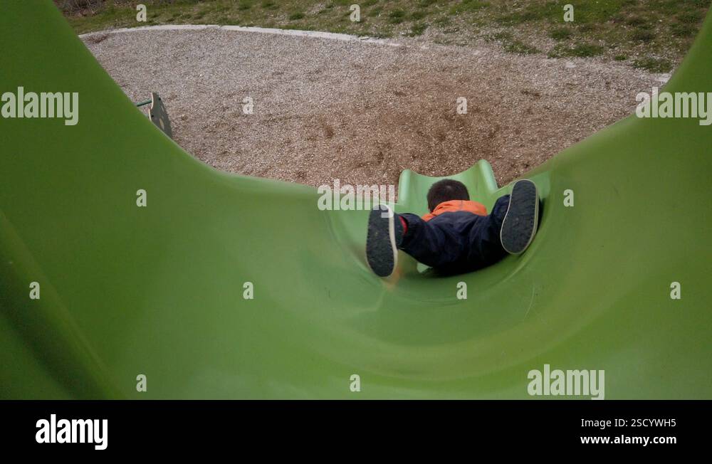 Young boy slides down play structure slide in autumn fall head first on ...