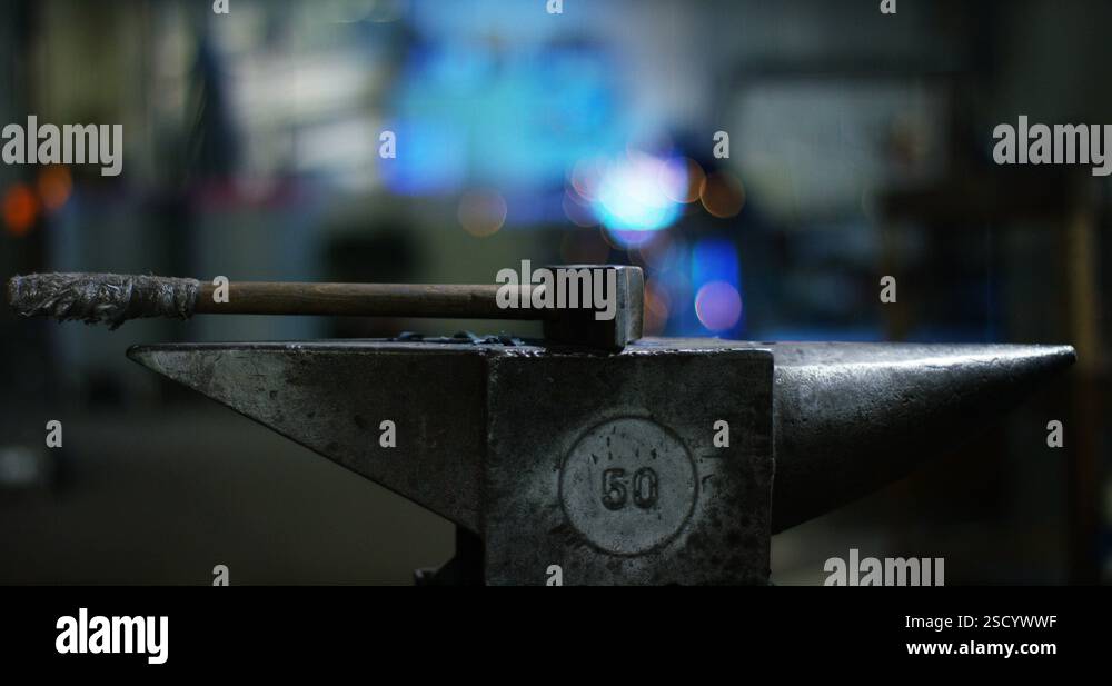 A blacksmith is working hot iron tapping it with a hammer on anvil ...