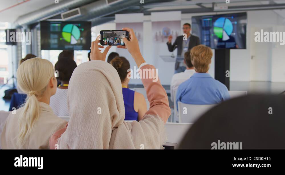 Woman in audience at a business conference filming with smartphone ...