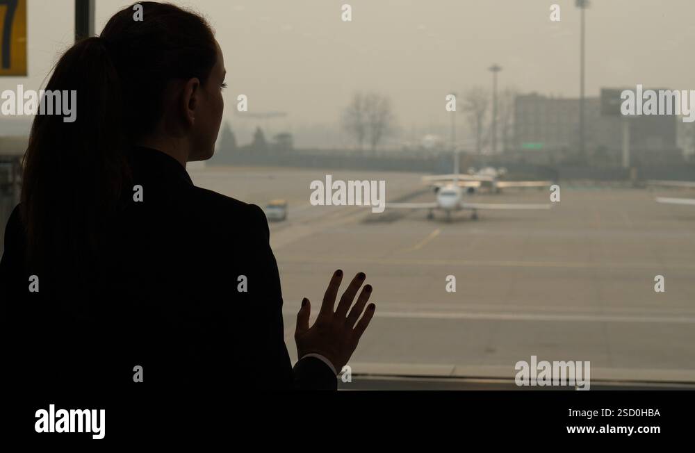 Thoughtful woman stay at window, look out to small bizjet plane parked ...
