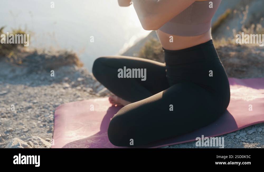 Part of woman sits lotus yoga position on mat and meditates outdoors ...