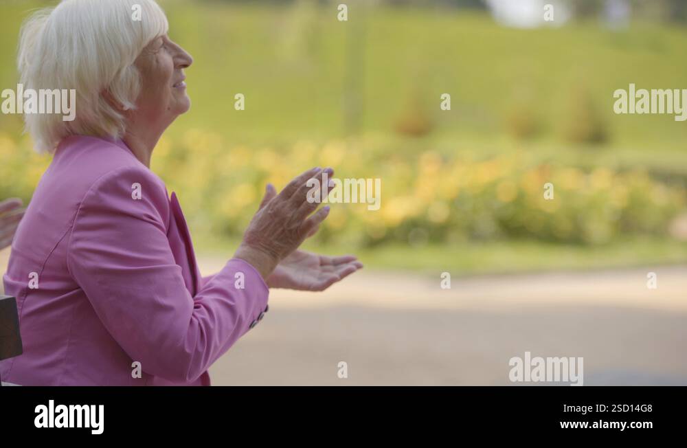 Side view of a nice blonde mature woman sitting in the summer park and ...