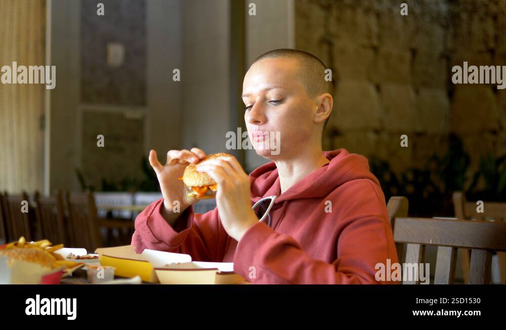 hungry bald woman eating a tasty burger in a fast food restaurant Stock ...