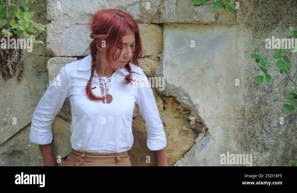 A girl in medieval village clothes walks along a ledge along the wall ...