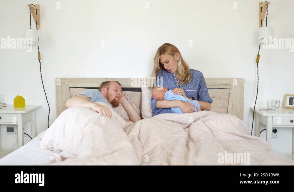 woman falls asleep rocking baby in her arms lying in bed next to her ...