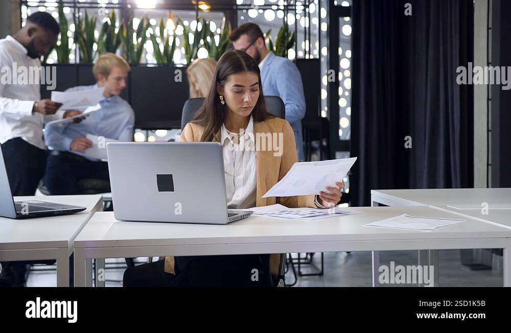 Beautiful experienced young female office worker comparing datas from ...