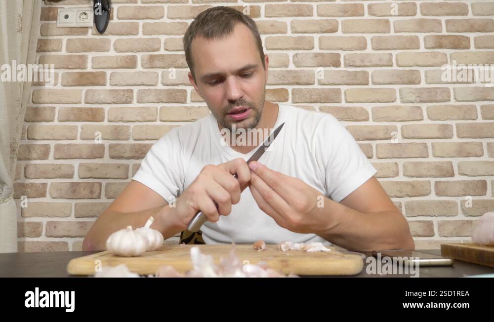 a man peels garlic sitting at a table on a background of a brick wall ...