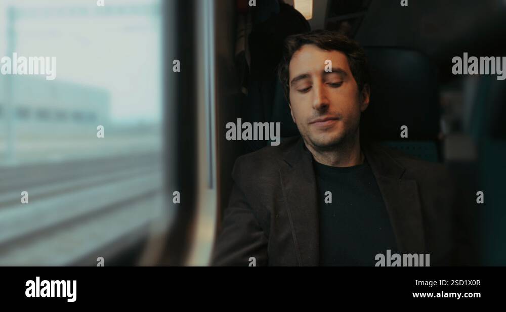 Commuter man putting on headphones while riding train and looking out ...