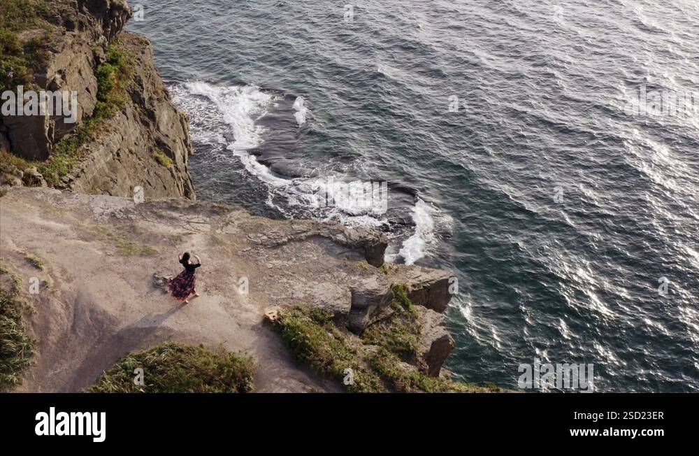 Top aerial view of gipsy woman dancing on high cliff peak above blue ...