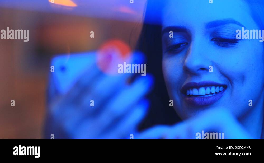 Real life laugh of Girl using cellphone at night next to blue neon sign ...