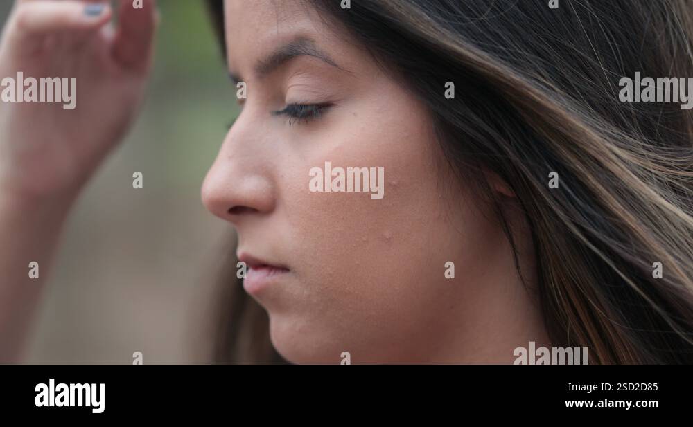 Woman outside at the park arranging hair, thoughtful pensive casual ...
