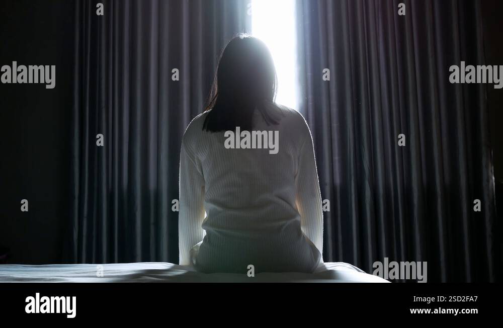 Rear of an Asian woman sitting and stretch lazily in the bright morning ...