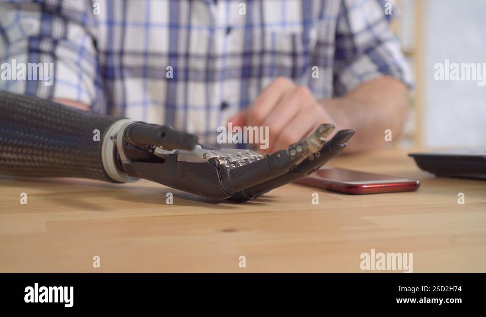 young man sitting at a table is setting up a cyber prosthetic arm ...