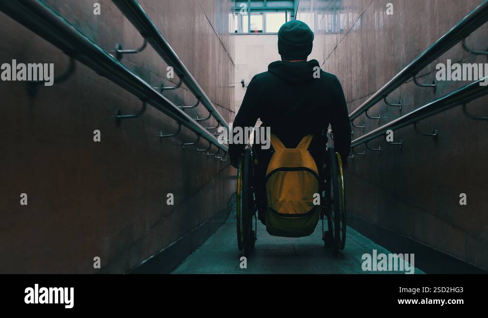 Disabled man in wheelchair getting down the long ramp in the subway ...