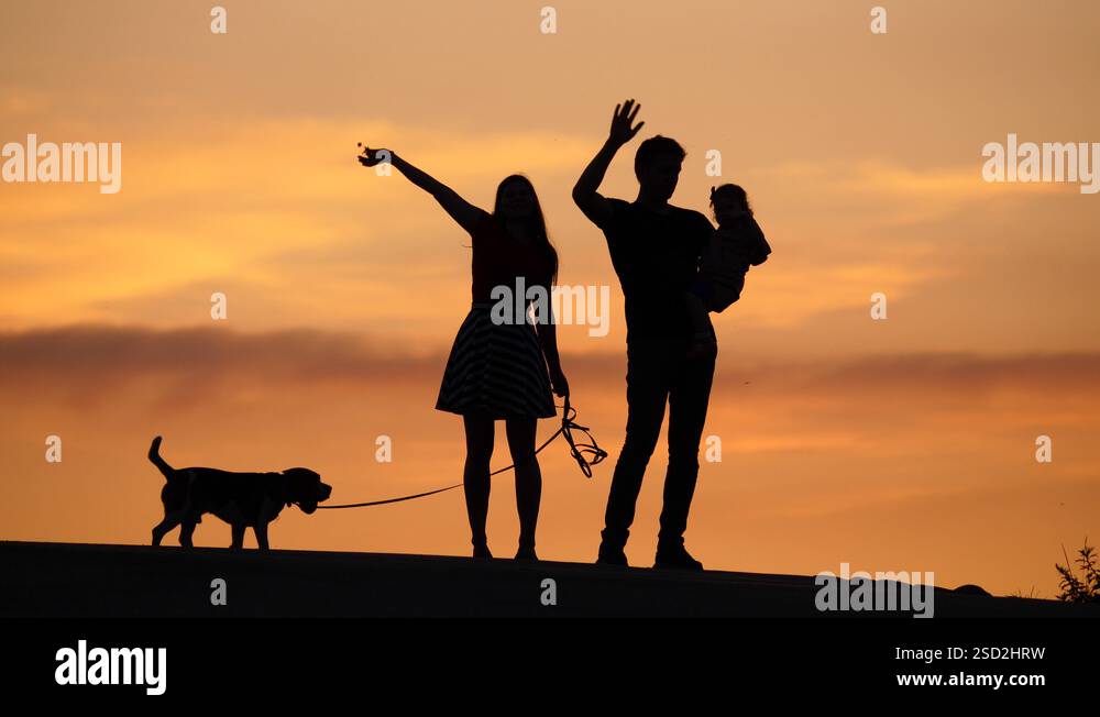 Couple with little child and dog wave goodbye, full length silhouetted ...