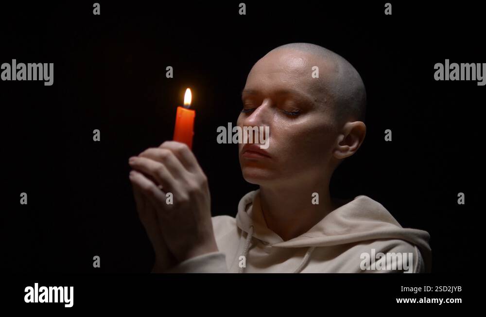 Portrait of a bald woman with a candle on a black background. copy ...