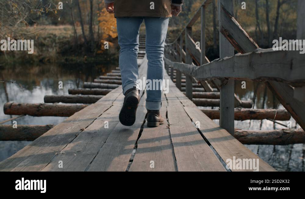 Legs/feet of man walking along suspension bridge over river, trekking ...