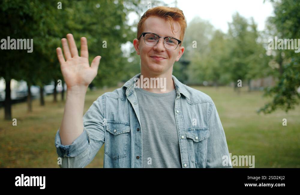 Portrait of attractive guy waving hand greeting people and smiling in ...