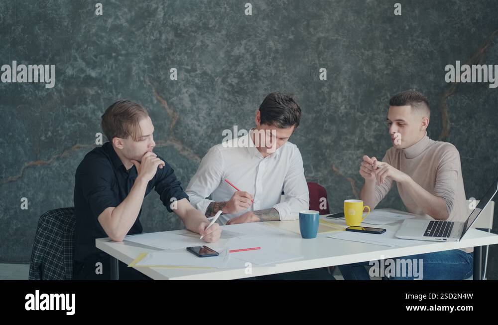 three men discuss a project and plan while sitting at a table in an ...