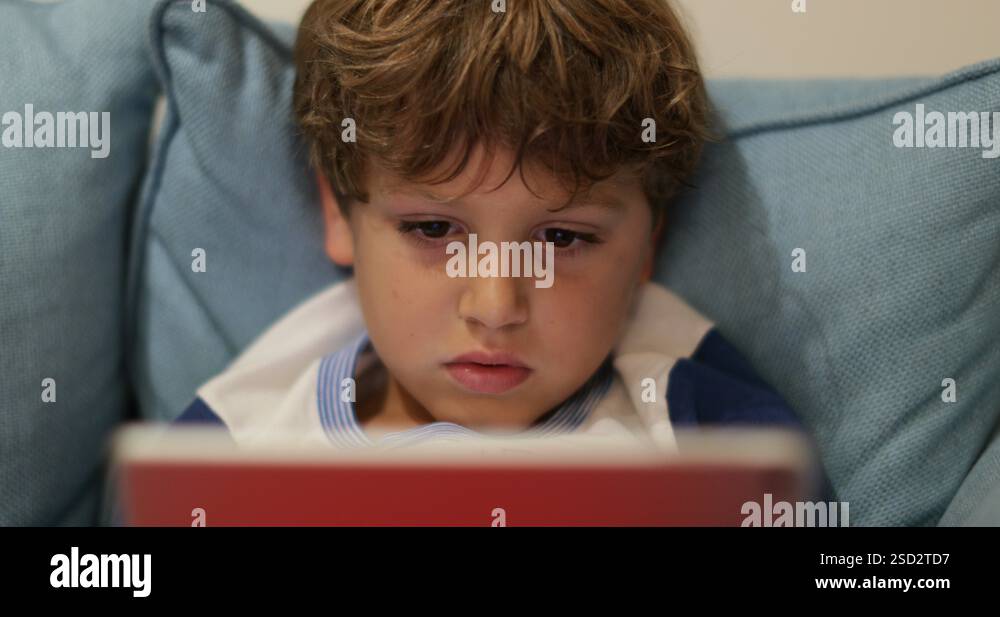 Closeup of child face hypnotized by tablet screen. Young boy in front ...