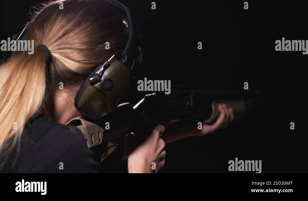 Woman aiming and firing shotgun with recoil, wearing ear protection in ...