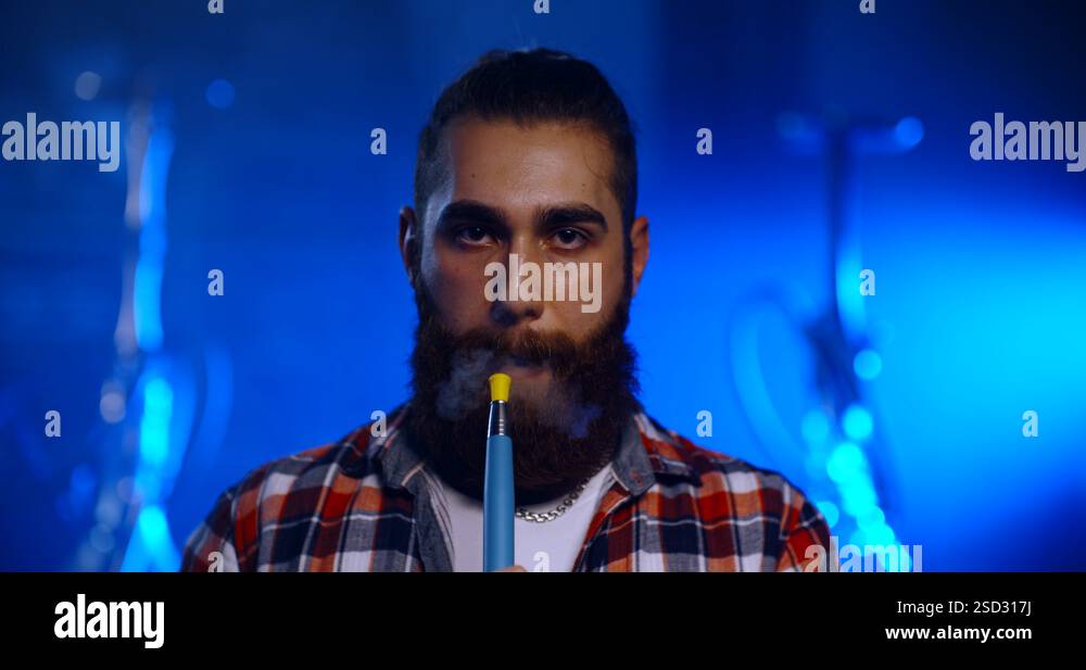 Young hipster guy looking at camera while smoking a hookah in a club ...