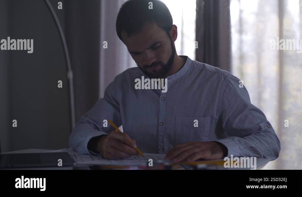 Young handsome Caucasian guy drawing blueprint with different pencils ...
