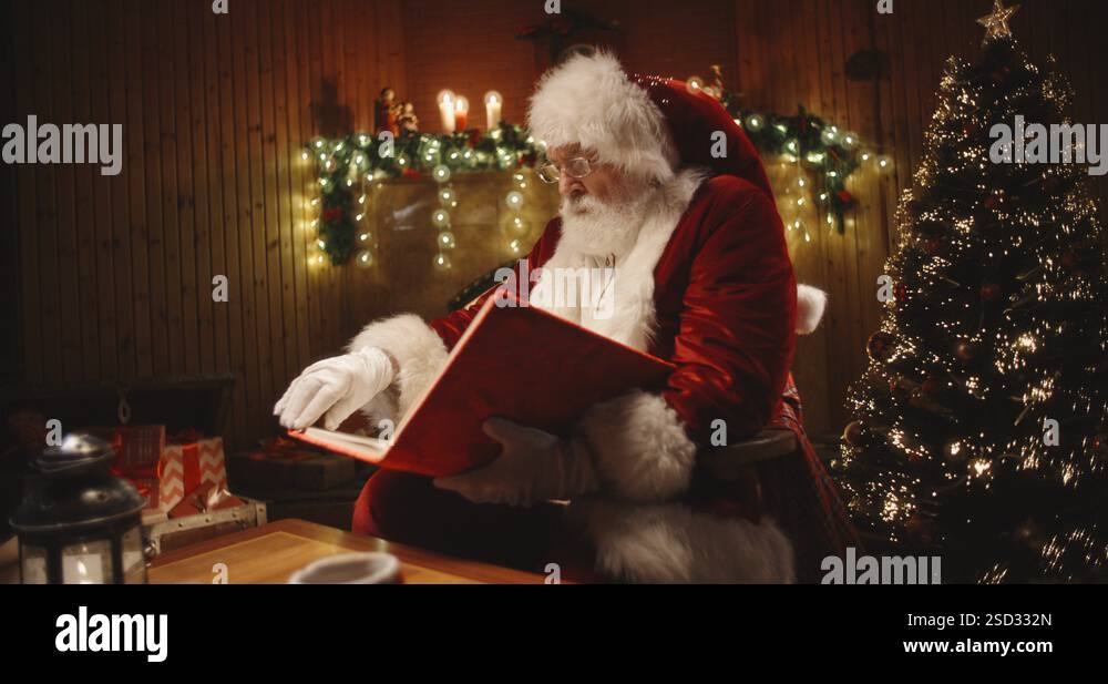 Joyful santa clause sitting in his rocker in decorated room, reading a ...