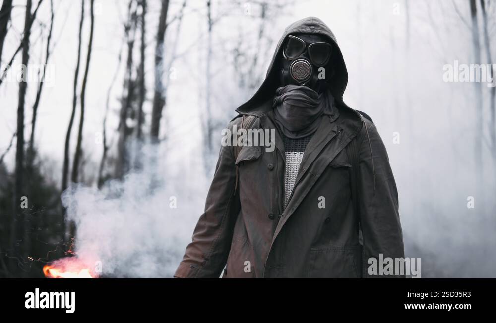 Man in gas mask standing in empty dead forest, holds red signal fire in ...