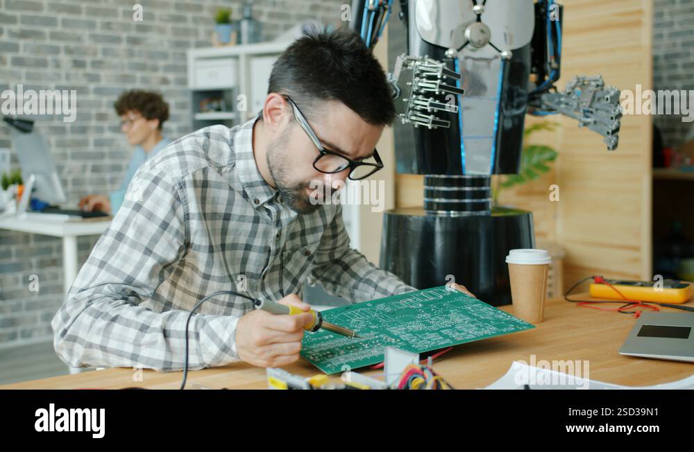 Male technician repairing microcircuit board with solderer making robot ...