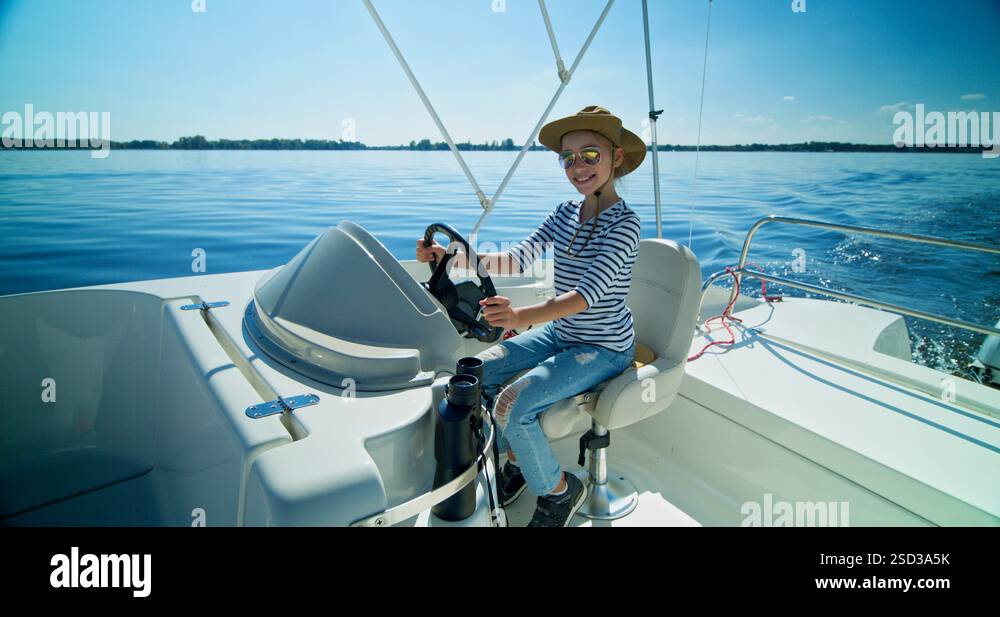 Teenager girl at helm of motor boat out at river, steering, smiling ...