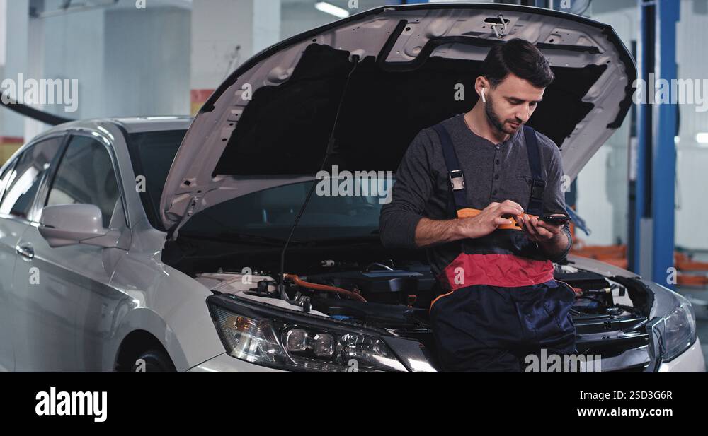Attractive mechanic guy in a uniform have a break check his phone he ...