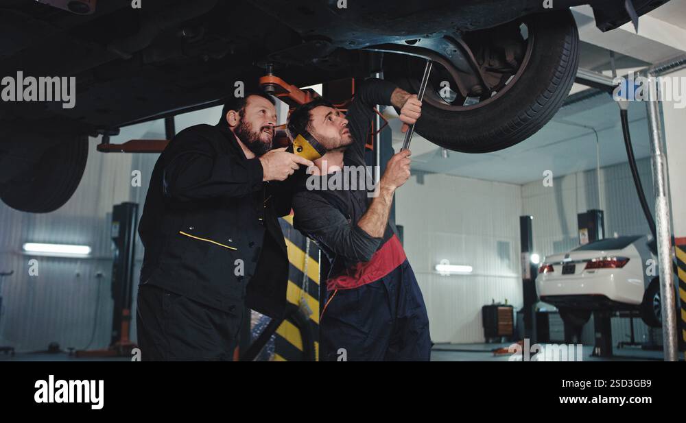 In a modern auto service center two mechanic in the uniform under the ...
