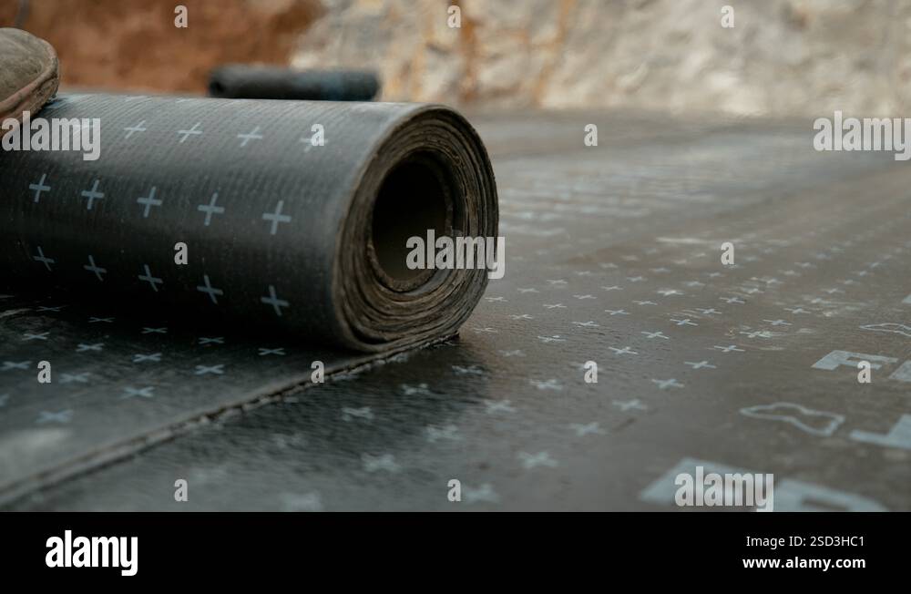 CLOSE UP: Worker rolls out tar paper with his foot while waterproofing ...