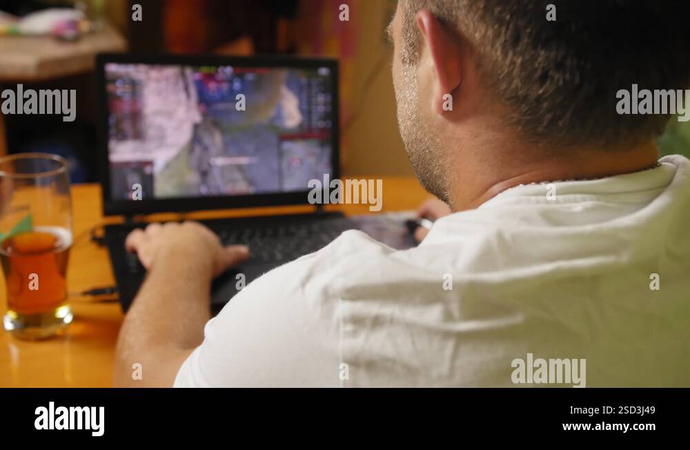 Man plays computer games on a computer and drinks beer from the glass ...