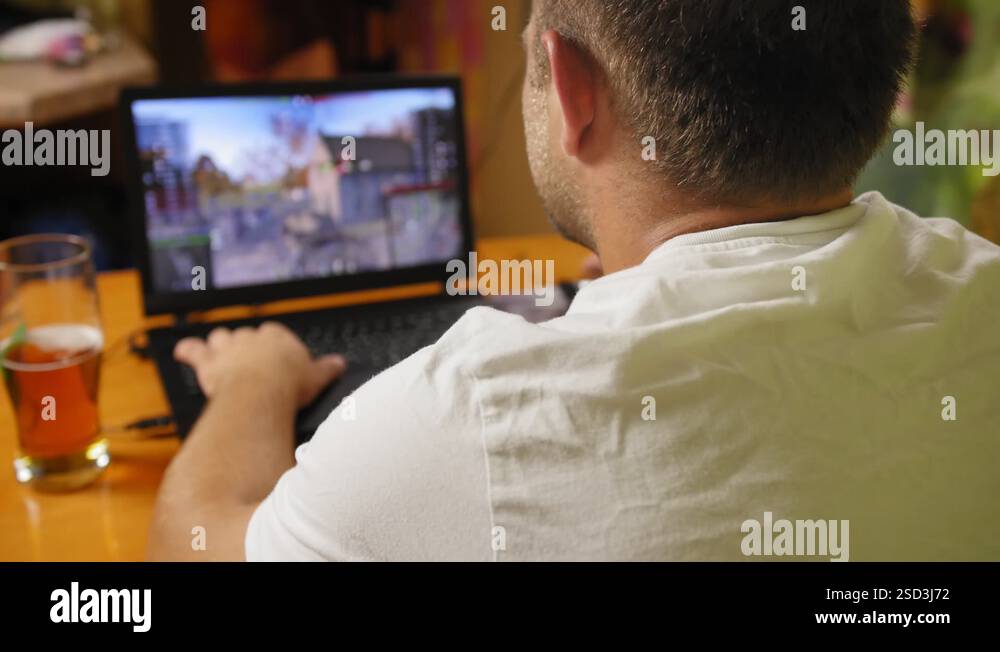 Man plays computer games on a computer and drinks beer from the glass ...