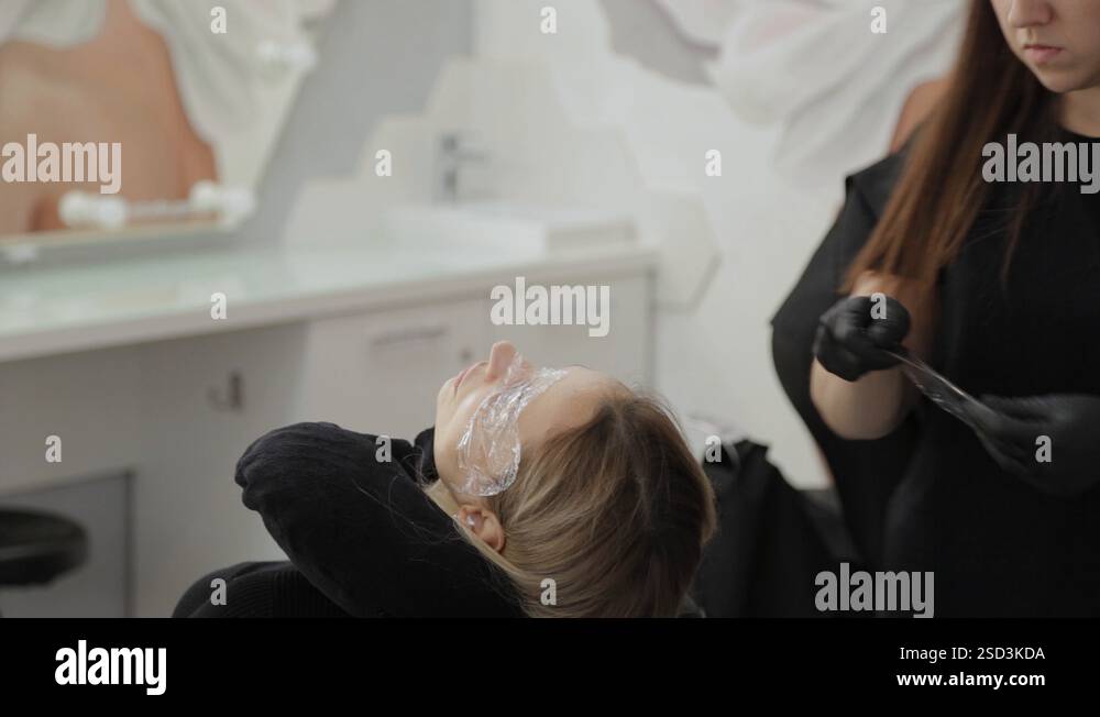Professional beautician in a beauty salon closes the eyes of the client ...
