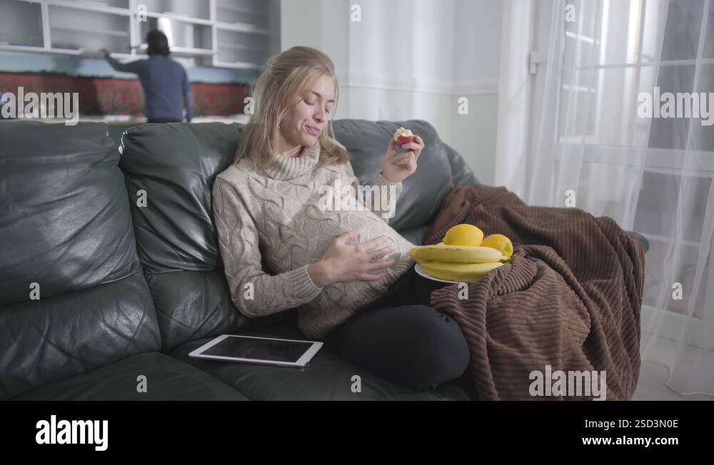 Pregnant Caucasian girl chewing apple and caressing her belly. Her ...