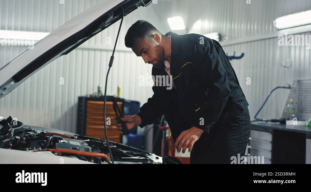 Mechanic young guy in a uniform concentrated working on a car fixing ...