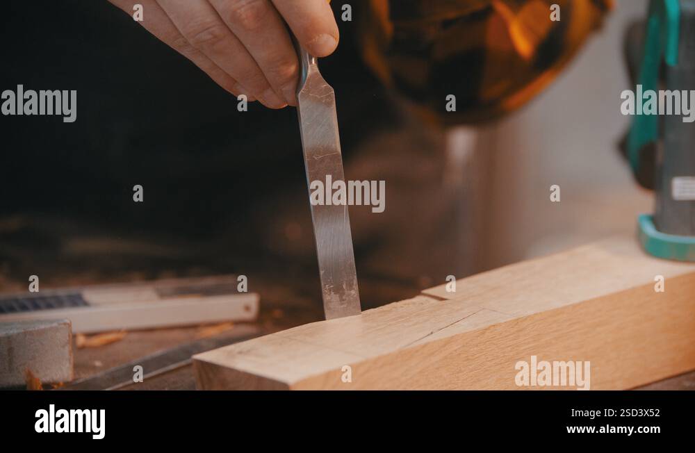 Carpentry - a man woodworker cutting out the recess on the wooden block ...