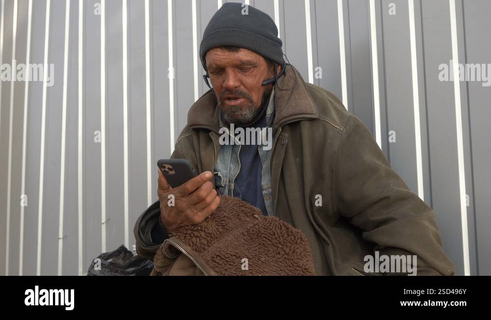 Homeless man listening to music with earphones and mobile phone singing ...