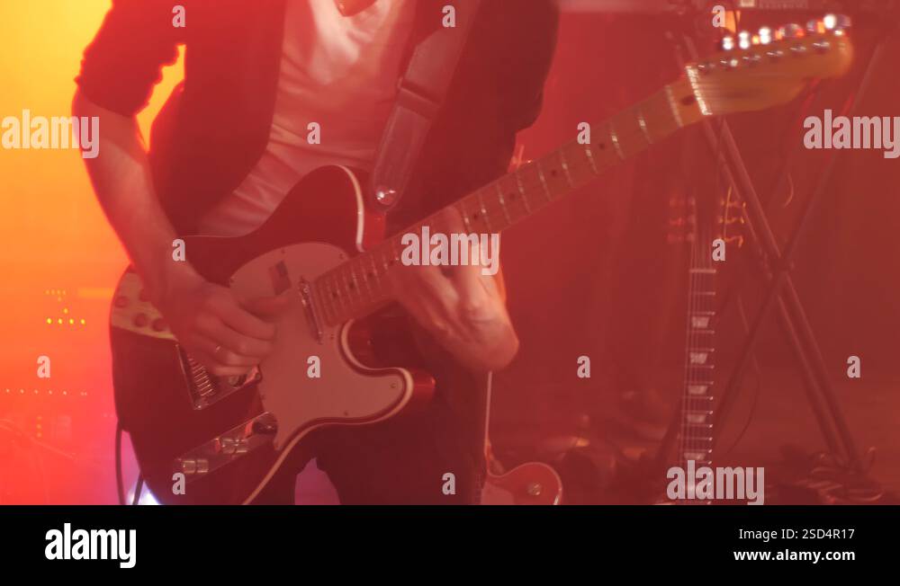 Guitarist in black shirt finger picking on stage filled with red and ...