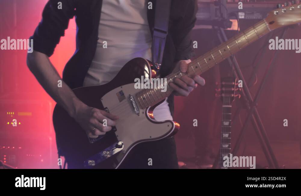 Guitarist in black shirt finger picking on stage filled with pink ...